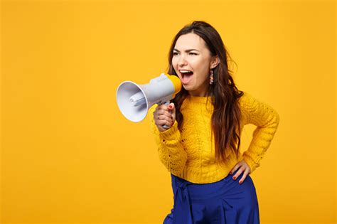 스웨터에 미친 젊은 여자 블루 바지 옆을 찾고 스튜디오에서 노란색 오렌지 벽 배경에 고립 된 확성기에서 비명 사람들은 진심으로 감정 라이프 스타일 개념입니다 복사 공간을
