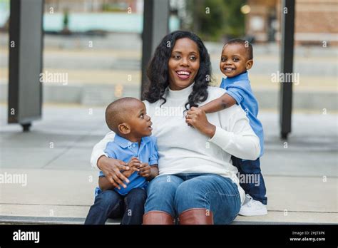 A Mom With Long Hair Sitting Outside With Her Two Young Sons Stock