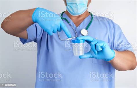 파란색 유니폼과 라텍스 장갑의 의사가 소변 샘플을 채취하기위한 빈 플라스틱 용기를 들고 있습니다 건강관리와 의술에 대한 스톡