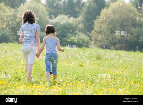 Two Girls Walking Away From Camera Holding Hands In A Field Full Of