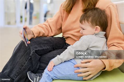 소아과 의사를 기다리는 클리닉에서 휴대 전화를 가진 엄마와 아기 손에 스마트폰을 든 아이 소년을 둔 부모 아이는 1 세 3 개월
