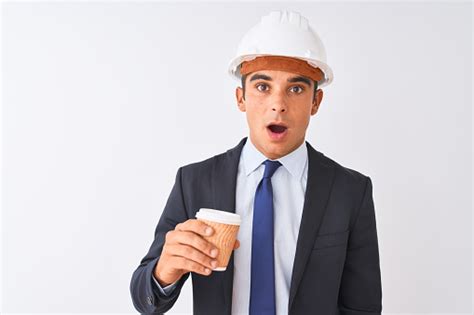 헬멧을 쓰고 있는 젊은 잘생긴 건축가 남자 고립된 흰색 배경에 커피를 마시고 깜짝 얼굴을 가진 충격에 무서워 두려움과 두려움 표정으로 흥분 감정에 대한 스톡 사진 및 기타