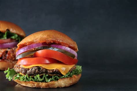 빵 빵 치즈버거 치킨 버거 고기 패티가 녹는 가공 치즈 조각 양상추 잎 얇게 썬 토마토 피클과 적양파 조각 검은색 배경 전경에 초점 복사 공간에 있는 두 개의 수제 햄버거의