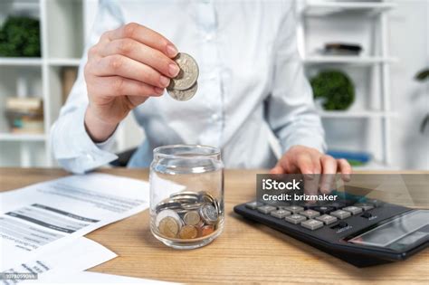 그녀는 유리 은행 항아리에 밝은 로프트 인테리어 워크스테이션 던져 동전에 테이블 뒤에 앉아 그녀의 Formalwear 셔츠에 은행 투자자 여자의 자른 사진 닫거나 냄비 계산