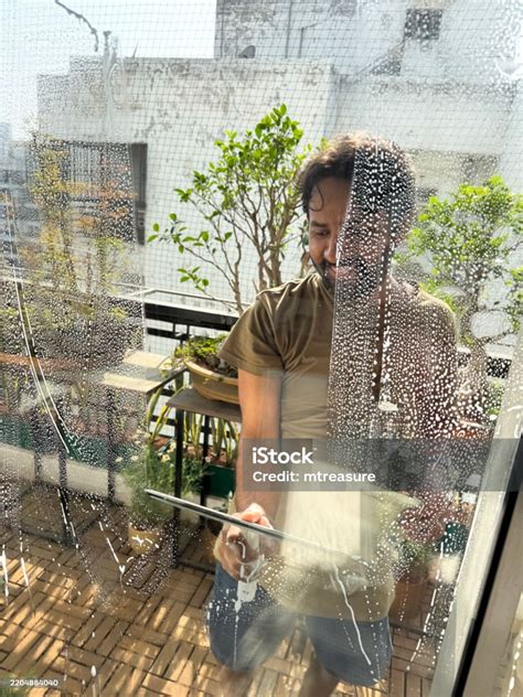 높은 주거용 발코니에 있는 인도 남자의 이미지 스퀴지 와이퍼 블레이드와 비눗물을 사용하여 유리창을 청소하는 창문 클리너 안전 난간 아파트 블록 배경 전경에 초점 30 34