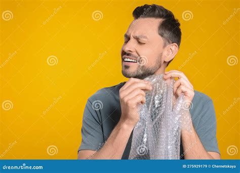 Man Popping Bubble Wrap On Yellow Background Space For Text Stress