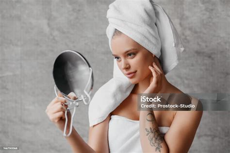 얼굴 치료 개념입니다 머리에 수건을 쓴 아름다운 백인 아가씨가 거울을 들고 그녀의 완벽한 부드러운 피부를 만지고 있다 20 24세에 대한 스톡 사진 및 기타 이미지 Istock