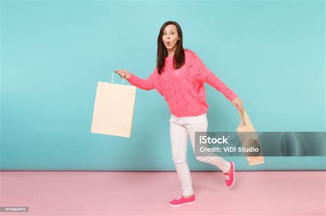 화이트 니트 장미 스웨터 바지 멀티 컬러 구매와 패키지 가방을 들고 여 인 초상화 스튜디오에서 밝은 핑크 블루 파스텔 벽 배경에 쇼핑 개념 모의 복사 공간을 격리 갈색