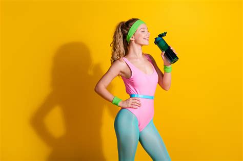 복고풍 운동복을 입은 쾌활한 여성이 생생한 노란색 배경을 배경으로 자신감과 기쁨으로 물병을 들고 있습니다 16 17 살에 대한 스톡 사진 및 기타 이미지 Istock