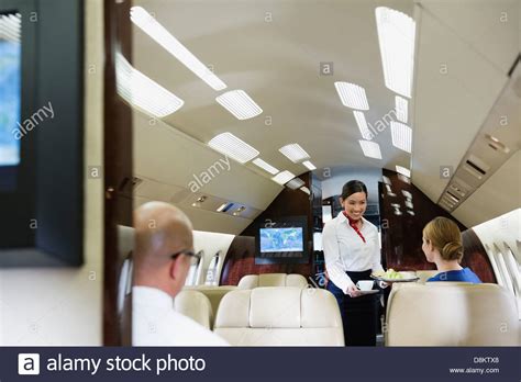 Flight Attendant Serving Food To Female Passenger In Airplane Stock