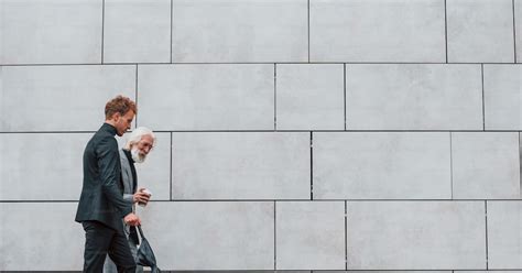 벽 근처의 잔디 위를 걷는다 우아한 옷을 입은 선배와 함께 젊은 남자가 함께 야외에 있습니다 사업의 개념 사진 Unsplash의 양복 이미지