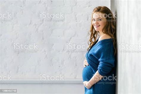 파란 바디콘 드레스를 입은 30주 임신한 여성이 하얀 벽에 머물러 있다 출산 휴가 임신 계획 출산 준비 개념에 대한 스톡 사진