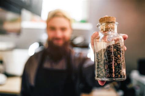 행복 한 젊은 바리 보류 유리 항아리 커피 콩 수염 그는 카메라에 그것을 보여줍니다 젊은 남자는 방에 서 있다 커피 콩에 대한 스톡 사진 및 기타 이미지 Istock