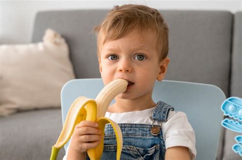 Menino Comendo Uma Banana Em Casa Foto Grátis