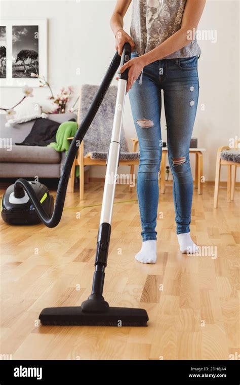 Low Section Of Teenage Girl Using Vacuum Cleaner On Hardwood Floor In
