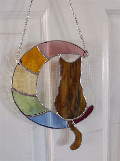 A Stained Glass Cat Hanging From A Chain On A White Door With A Wooden