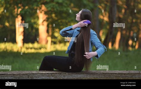 A Young Girl Strokes Her Long Hair While Sitting In The Park Stock