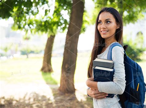 خرید و قیمت عکس با کیفیت دختر با لبخند و کتاب بدست در فضای سبز ترب