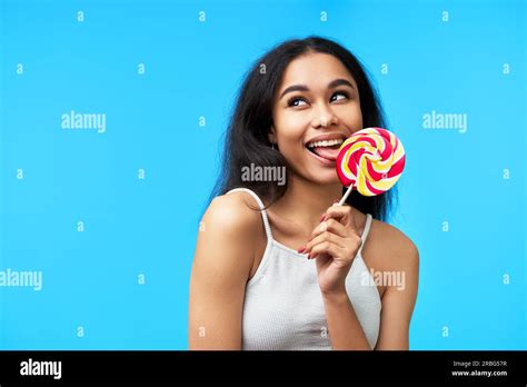 Happy Young Black Woman Licking Colorful Lollipop On Blue Background Food Fun Concept Stock