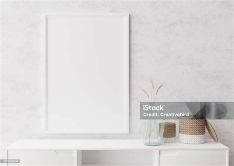 현대 거실의 흰색 벽에 빈 수직 사진 프레임 미니멀한 스칸디나비아 스타일로 인테리어를 모의하세요 그림을 위한 여유 공간 콘솔 등나무 바구니 꽃병에 말린 잔디 3d 렌더링 0