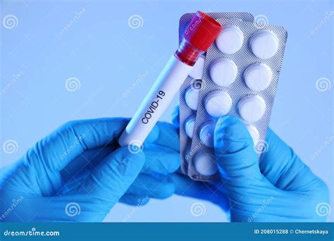 Scientist Holding Test Tube With Blood Sample And Pills On Blue