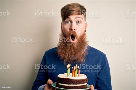 깜짝 얼굴 두려움과 두려움 표정으로 흥분 충격에 무서워 고립 된 배경에 불타는 촛불과 함께 생일 케이크를 들고 수염아일랜드 빨강 머리 남자 생일 케이크에 대한 스톡 사진 및