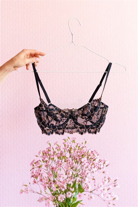 Woman Hand Holding Bra On Pink Background With Flowers Lingerie In