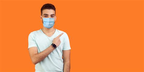 여기 봐 왼쪽을 가리키는 왼쪽 텍스트에 대 한 빈 공간을 가리키는 캐주얼 흰색 티셔츠에 의료 마스크와 갈색 머리 남자의 초상화 광고 보호 마스크에 대한 스톡 사진 및 기타