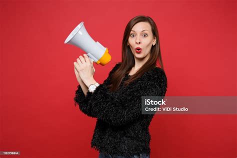 깜짝 놀란의 초상화 검은 모피 스웨터 스튜디오에서 밝은 빨간색 벽 배경에 고립 된 확성기를 들고 서 있는 젊은 여자 사람들은