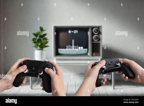 Two Players Holding Gamepads In Front Of A Retro Tv Displaying A Simple