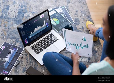 Biracial Woman Sitting On Floor Using Computer With Statistical Data On Screen Business