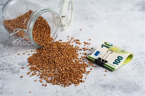 메밀은 유리 항아리에서 쏟아져 나와 회색 배경에 돈을 쌓았습니다 인플레이션 식량 위기 개념 0명에 대한 스톡 사진 및 기타