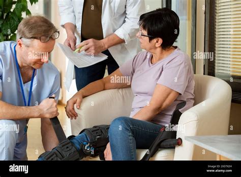 A Male Nurse Helps To Put A Bondage Medical Splint Knee Brace On The Leg Of An Elderly Female