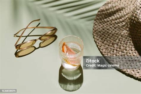 여름 플랫에는 밀짚 모자 선글라스 및 자몽 조각이있는 물 한 잔이 야자수 잎 그림자 태양 및 햇빛이있는 녹색 배경에 놓여 있습니다 휴가 휴일 여름 창조적 인 최소 개념