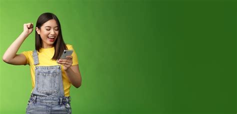 Premium Photo Triumphing Cute Joyful Asian Girl Hold Smartphone Fist
