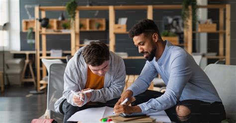 다운 증후군을 앓고있는 젊은 행복한 남자와 그의 가정교사는 학교에서 실내에서 공부하고 있습니다 사진 Unsplash의 교육 이미지