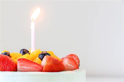신선한 딸기 블루 베리 및 망고를 얹은 맛있는 생일 케이크 과일 케이크의 일부와 불꽃으로 점화 된 단일 라이트 핑크 촛불의