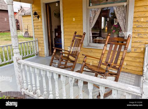 A Pair Of Old Wooden Rocking Chairs Sit On The Painted Wooden Porch Of