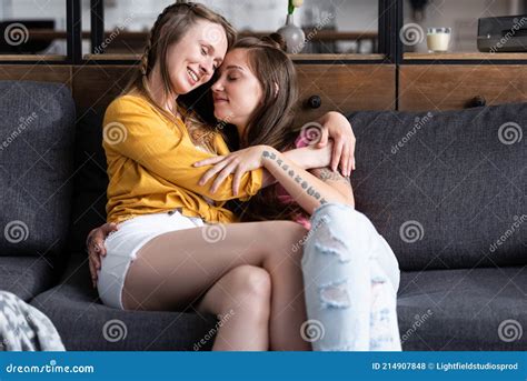 Two Pretty Lesbians Embracing While Sitting On Sofa In Living Room