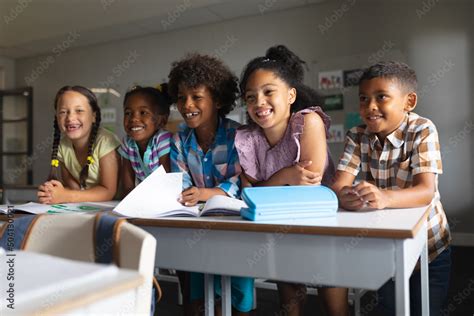 Happy Multiracial Elementary School Students Sitting At Desk In