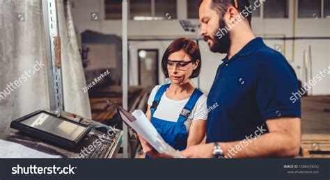 Female CNC Machine Operator And Industrial Engineer Checking Product Drawing In Industrial