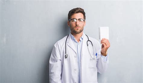 스마트 얼굴 심각한 생각에 자신감 표현 회색 그런 지 벽 잡고 빈 노트북에 잘생긴 젊은 의사 남자 감정에 대한 스톡 사진 및