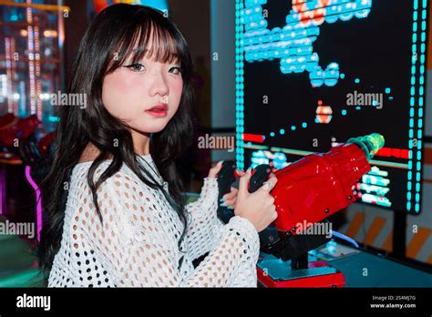Asian Gen Z Girl Enjoys An Arcade With Vibrant Lights Playing A Retro Video Game Her Focus Is