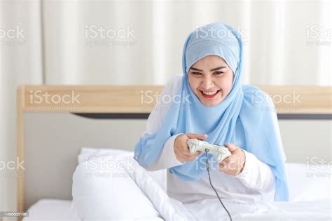 Vdo 게임 콘솔 스테이션 개념입니다 하얀 무슬림 잠옷을 입고 침대에 앉아 조이스틱을 들고 흥미진진한 게임을 하는 활동적인