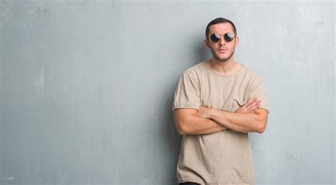 교차 팔과 얼굴에 선글라스 의심과 긴장 Disapproving 식 입고 회색 그런 지 벽에 젊은 백인 남자 부정적인 사람입니다 감정에 대한 스톡 사진 및 기타 이미지