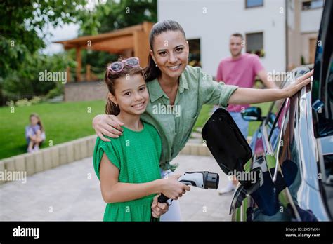 Happy Mother Showing Her Little Daughter How To Charge Their Electric
