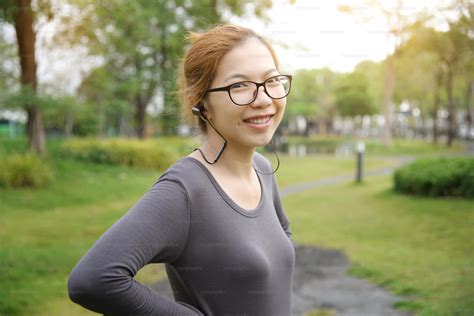 회색 운동복을 입은 행복한 젊은 아시아 여성은 아침에 야외에서 이어폰으로 음악을 들으며 웃고 있다 공원에서 여성 운동 건강