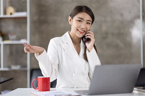 스마트 폰으로 이야기하고 사무실에서 일하는 사업가 그의 직장에 앉아있는 아시아 여성 비즈니스 Brand Name Smart