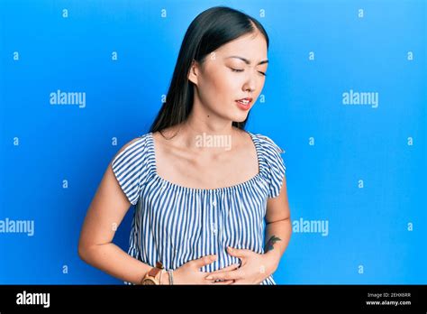 Young Chinese Woman Wearing Casual Striped T Shirt With Hand On Stomach