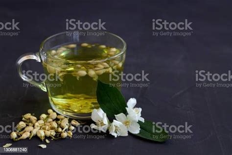 재스민 차 검은 테이블에 재스민 신선한 꽃 뜨거운 허브 차 한 잔 건강한 라이프 스타일 검은 색 배경에 마른 잎이있는 녹차 유리